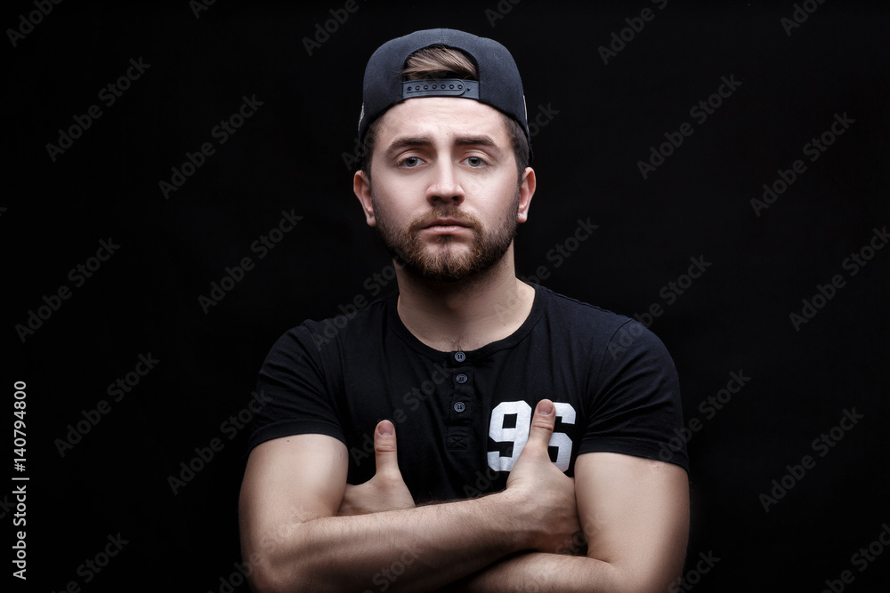 portrait of handsome young man in black shirt and cap on black ...