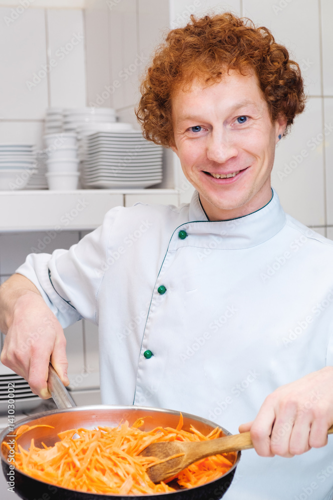 Male chef with red hair in the kitchen. Prepares stewed carrots Stock ...
