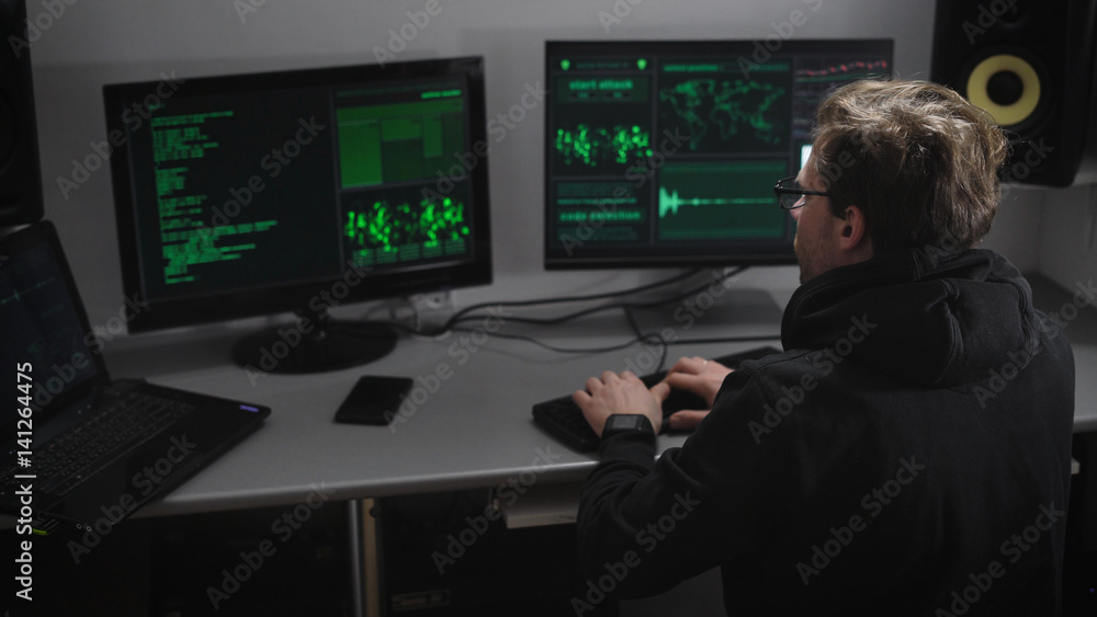 Villain hacker analyzes illegally obtained data on the monitor screens for creating spy software ...