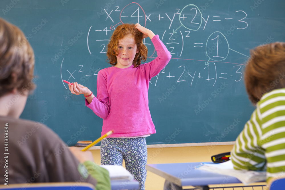 Primary schoolgirl scratching her head at equation on classroom ...