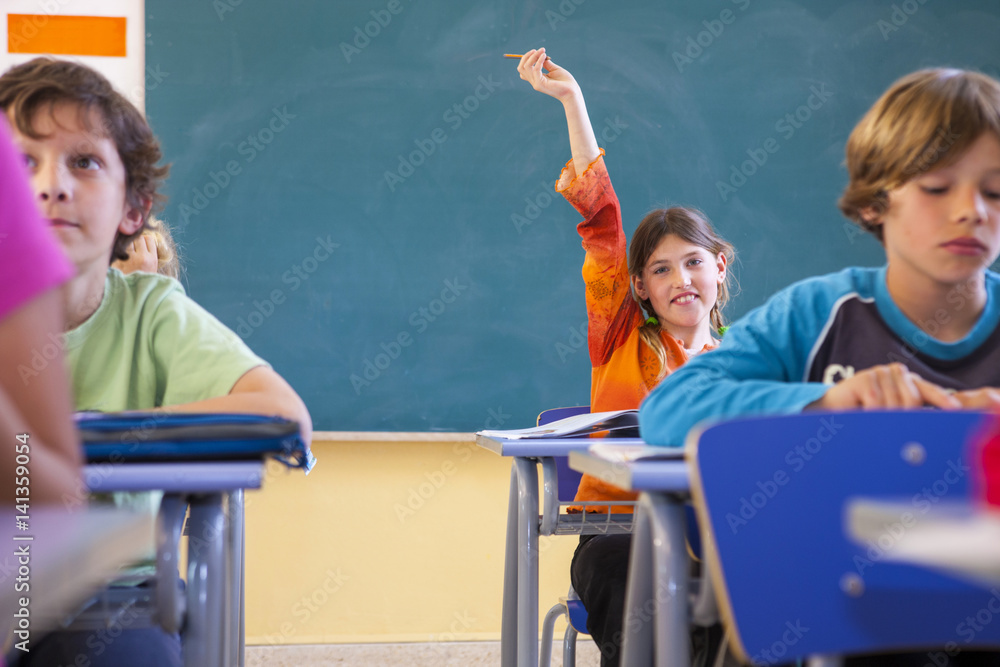 Primary schoolgirl with hand raised in classroom Stock Photo | Adobe Stock