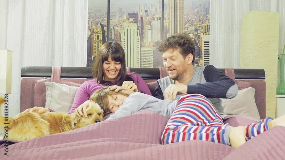 Family cuddling in bed in the morning happy with little dog and child ...