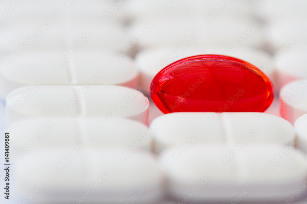 A single red medicine capsule standing out amongst rows of white, pain ...