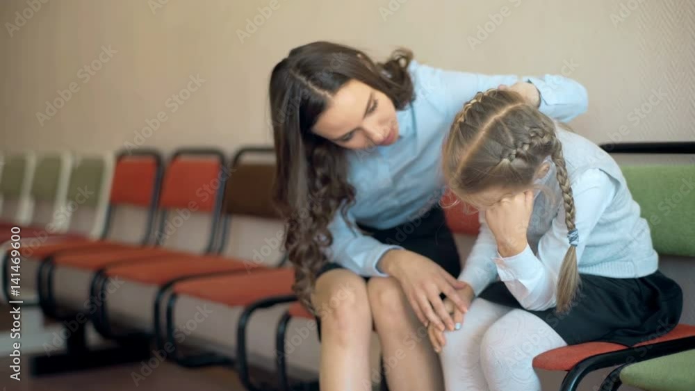 A female teacher sits consoling a young school sad girl in the corridor ...
