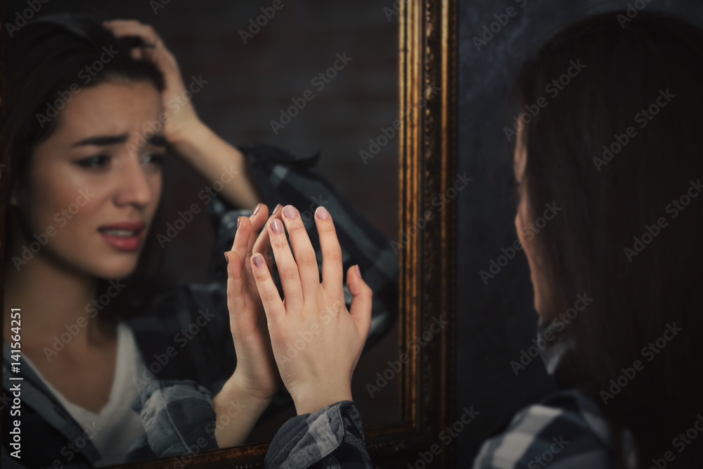 Depressed young woman looking on her reflection in mirror Stock 사진 ...