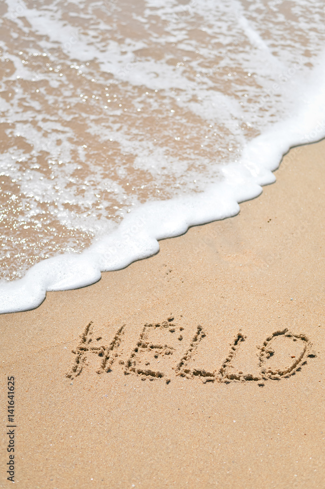 Hello sign word drawn on the outside sand beach with the soft foam wave ...