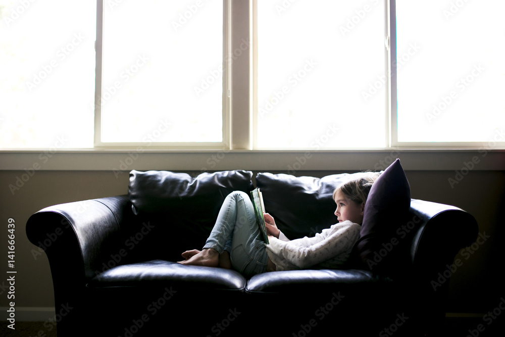 Side view of girl reading book while lying on sofa at home Stock Photo ...