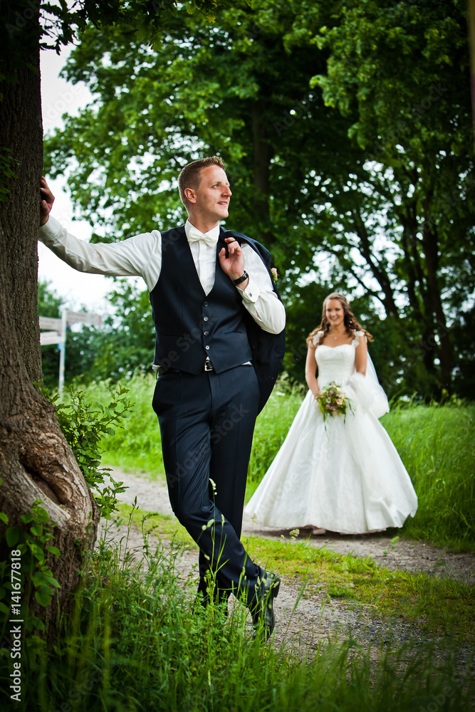 Groom is standing on the oak tree after the marriage with his cute and ...