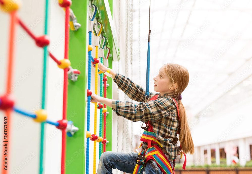 little girl climbing the wall on safety ropes in entertainment center ...