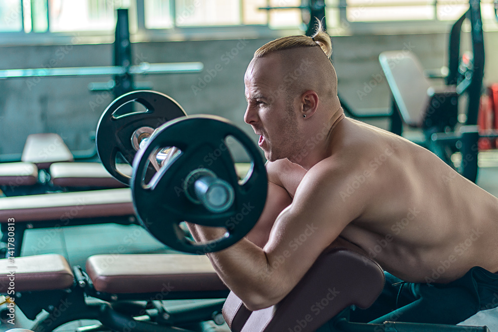 Strong athletic man makes exercise with the preacher curls in the gym ...