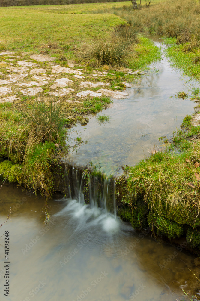 Small stream running on a green meadow with stones and smooth water ...