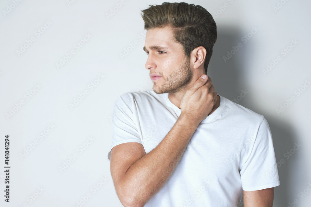 Sad unhappy young man in casual white t-shirt suffering from neck pain ...
