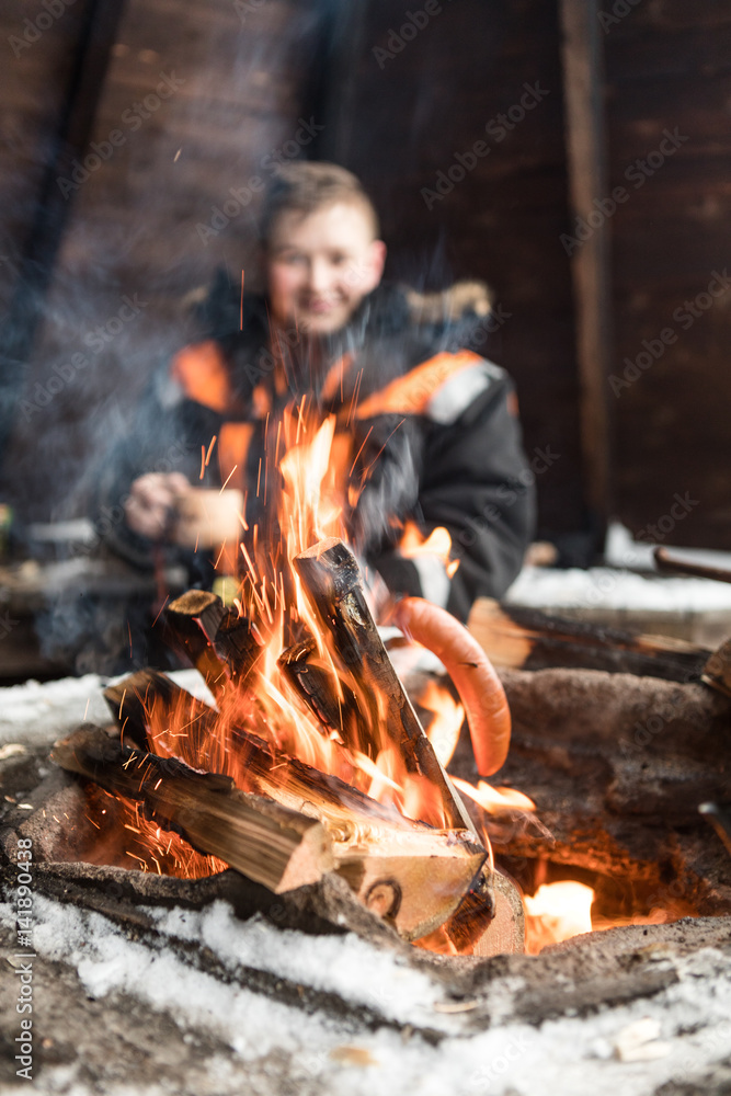 Foto de Man cooking sausage sitting in front of open fire in log cabin ...