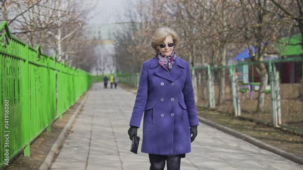 An attractive middle-aged woman walking down the street. Slow motion ...