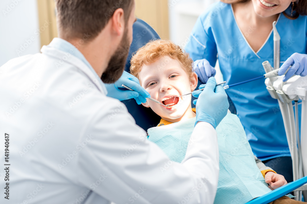 Children's dentist examinating baby teeth of a young boy sitting on the ...
