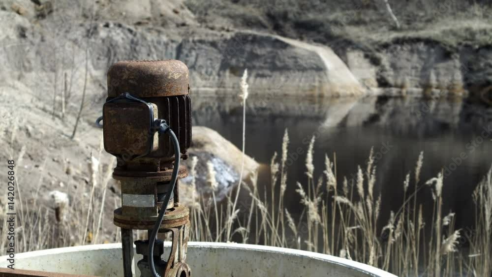 A rusty old vertical pump or sump pump sitting abandoned in front of a ...