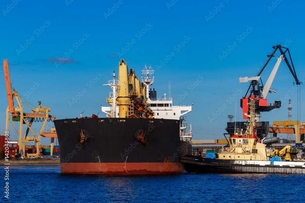 Foto de Black cargo ship mooring at the port with tug ship support do ...