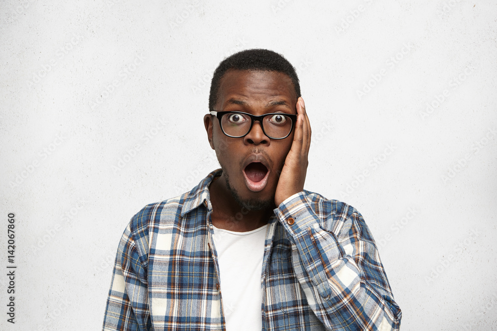 Headshot of young bug-eyed dark-skinned man in glasses touching his ...