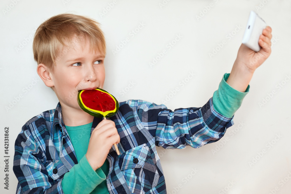 Adorable little boy licking big colorful lollipop and making selfie by ...