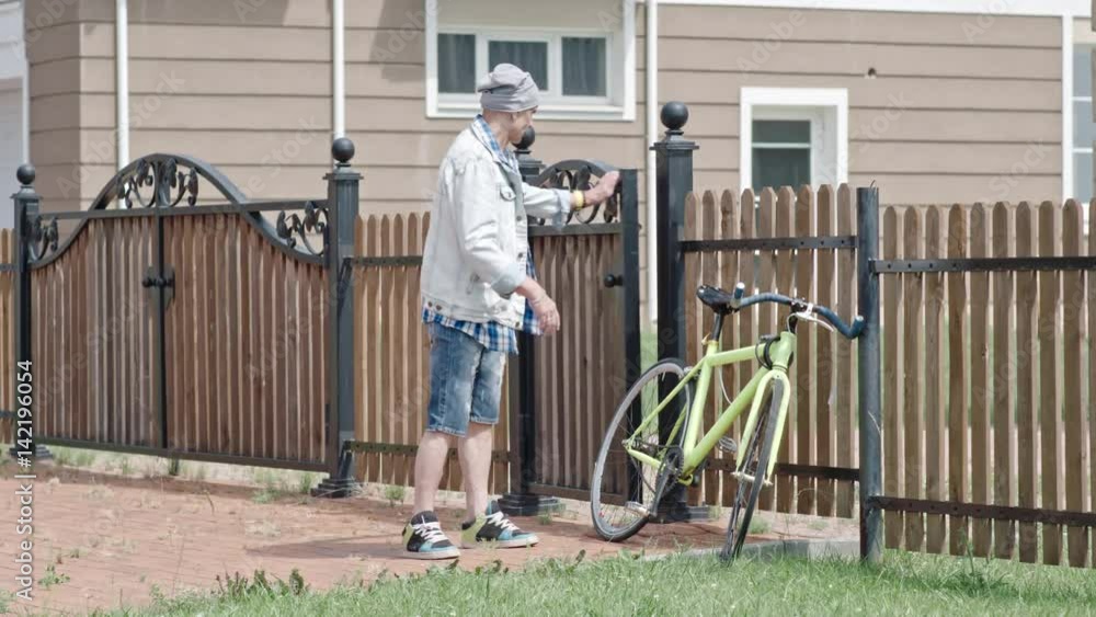 Stylish senior man walking out of house gate, sitting down on bicycle ...
