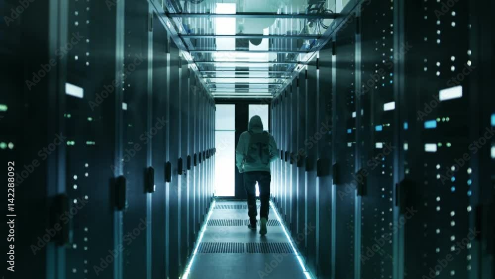 Following Shot of a Hacker in a Hoodie Walking in Data Center and ...