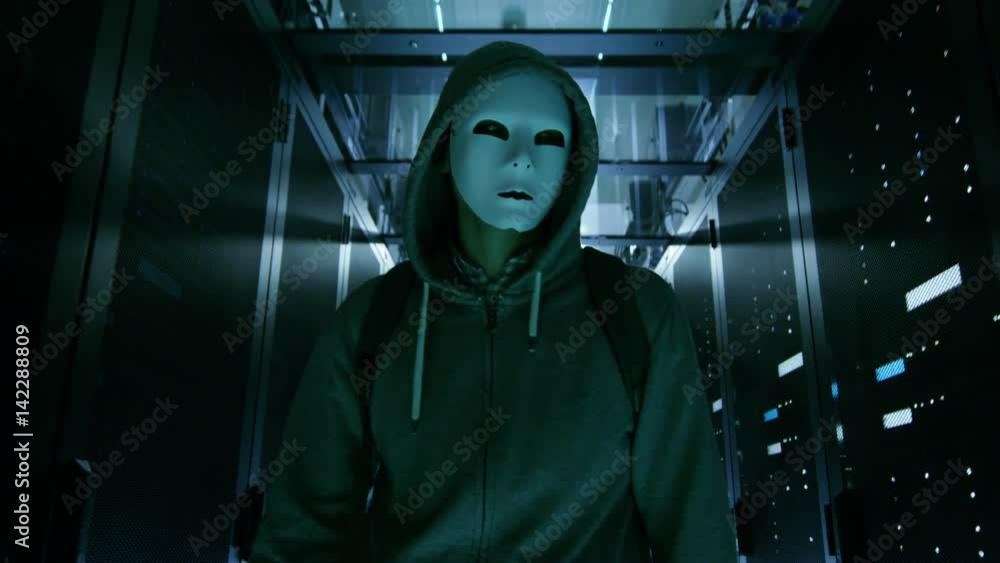 Masked Hacker in a Hoodie Walks Through Corporate Data Center with Rows ...