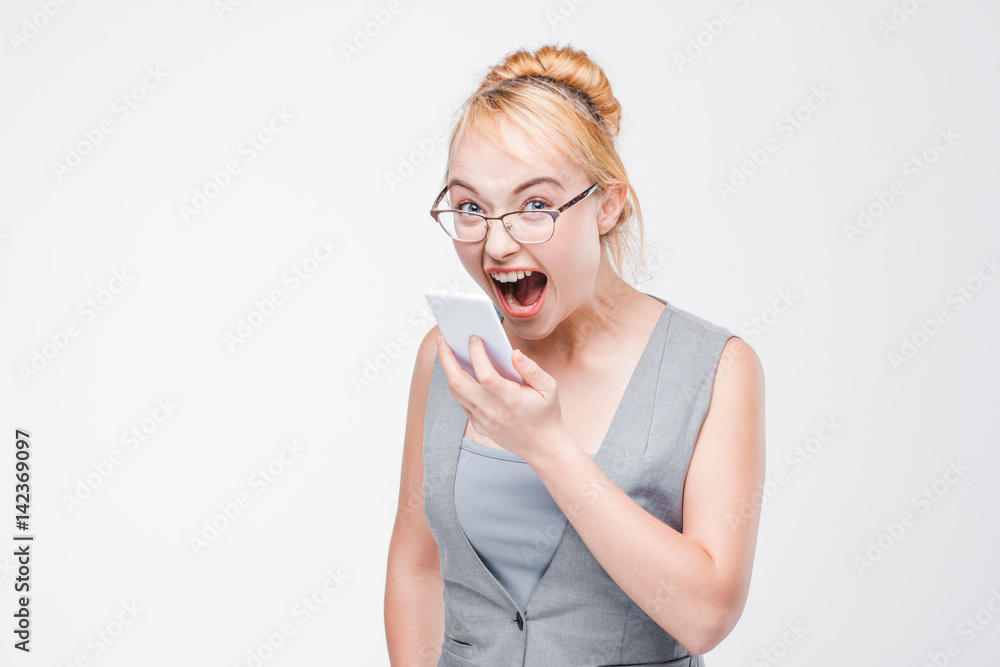 Angry young woman in glasses with mobile phone looks furious, enraged ...