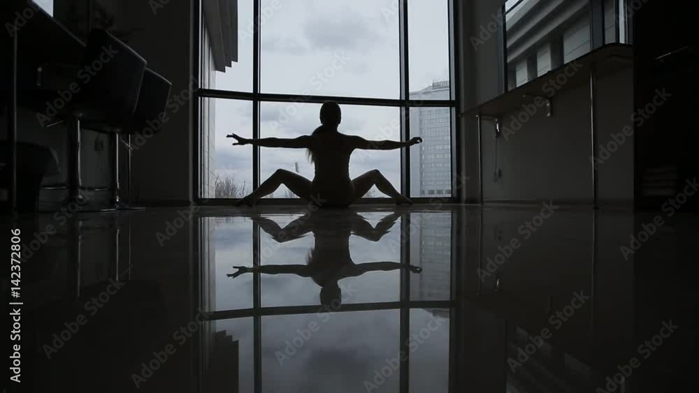 Silhouette and reflection of a young gymnast by the window. A girl in a ...