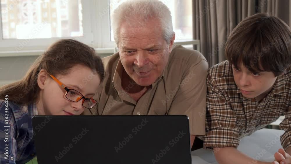 Little girl in glasses help her grandpa to type on laptop. Senior gray ...
