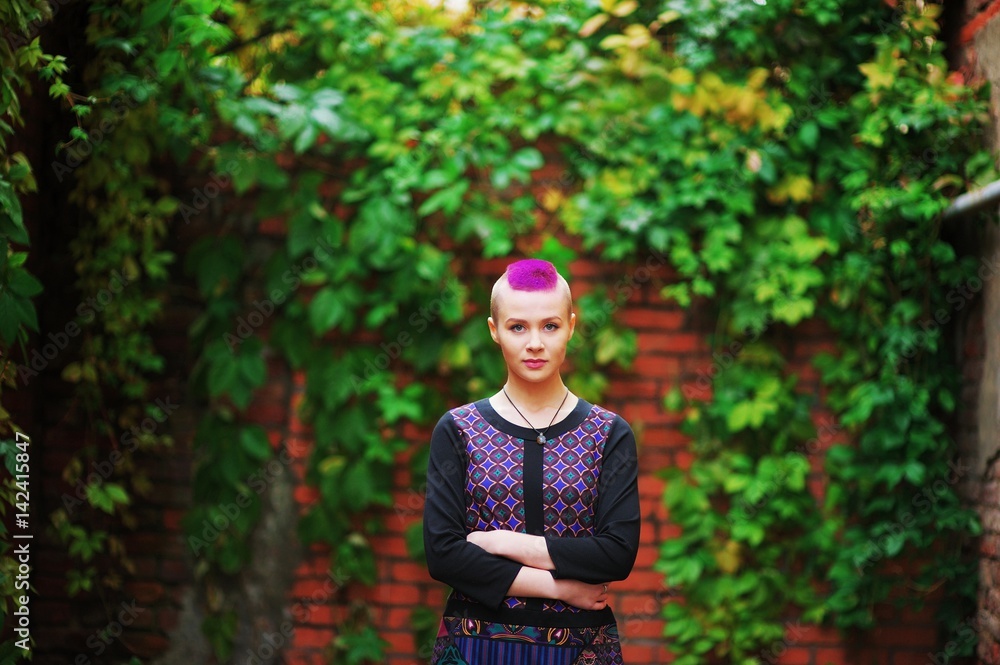 Beautiful punk girl with a purple mohawk standing against a background ...