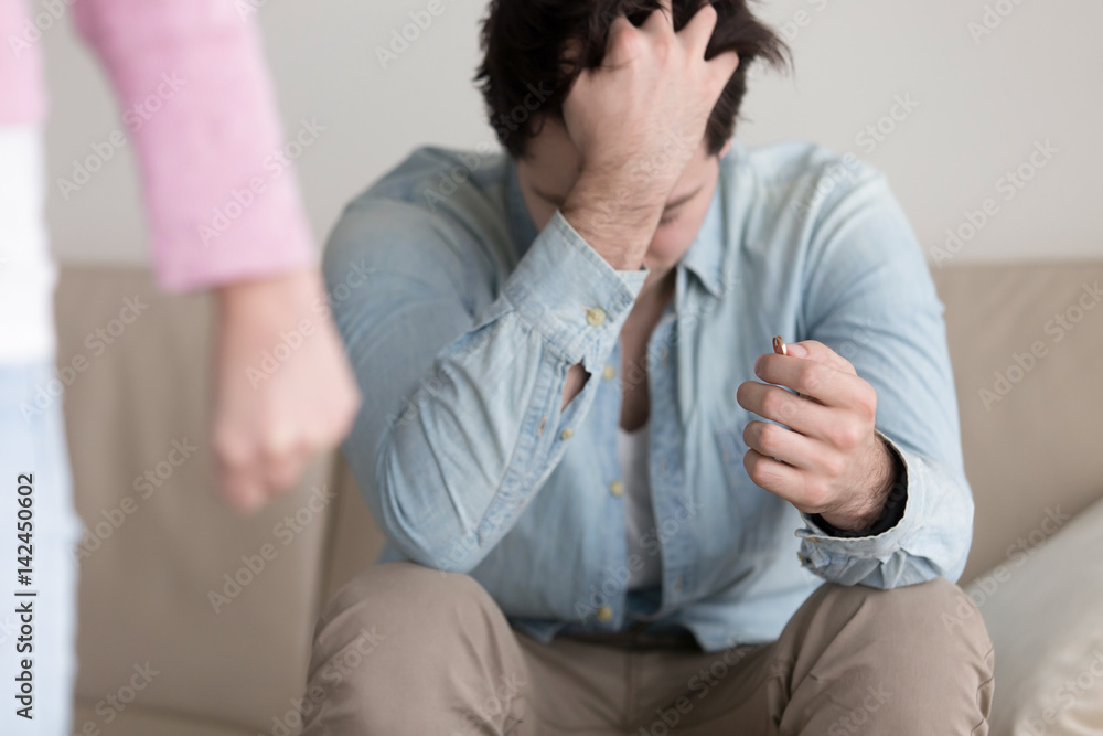 Young sad man sitting indoors with wedding ring in hand, wife breaks up ...