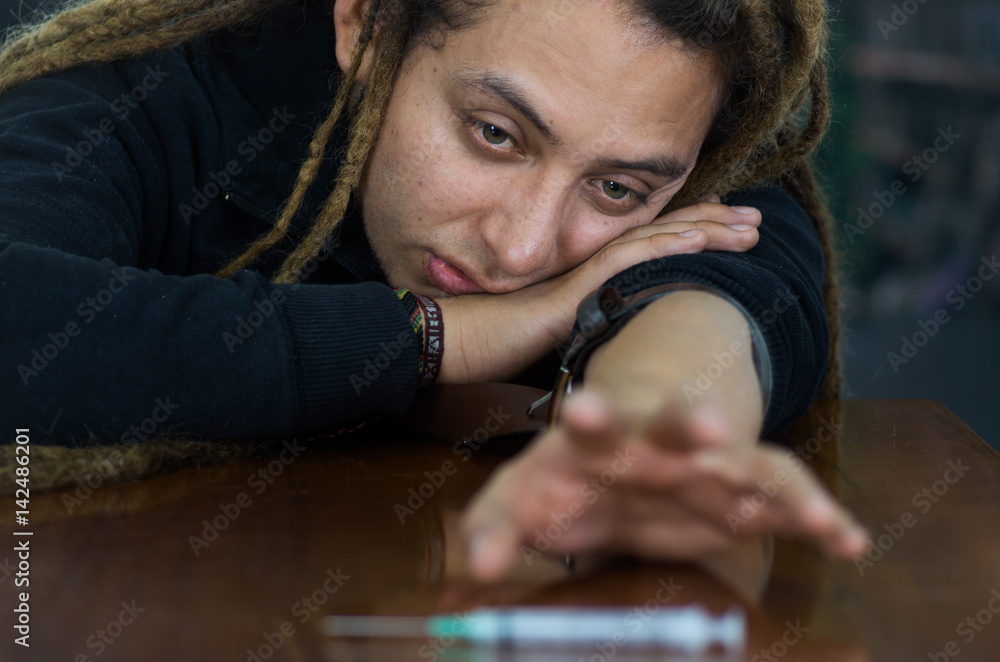 Man lying over table with dopey facial expression, reaching for syringe ...
