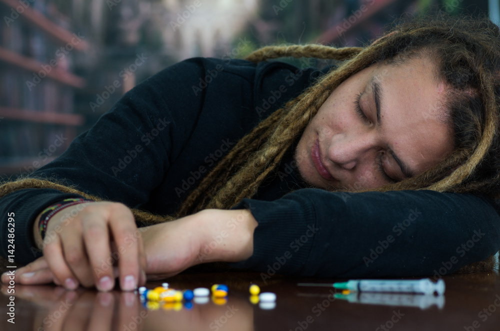Man lying over table with dopey facial expression, colorful pills and ...