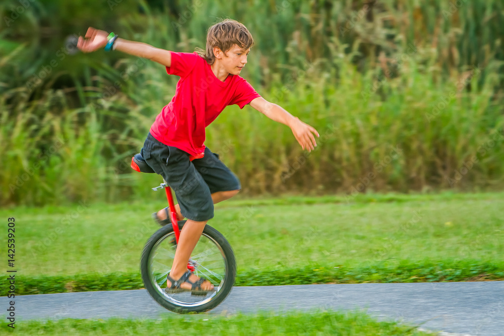 outdoor portrait of young boy riding a unicycle on natural background ...