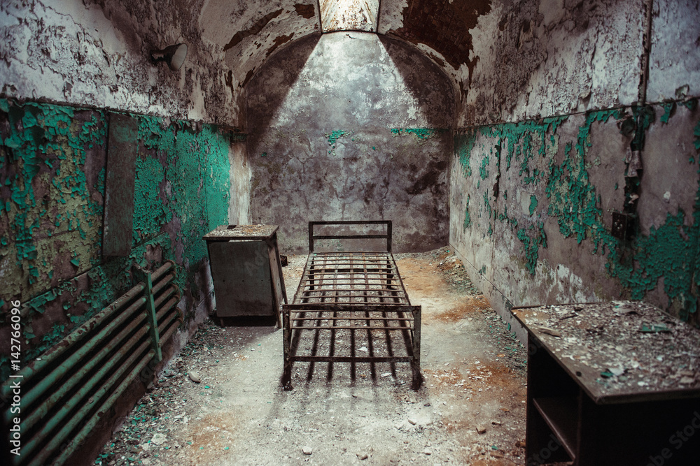 Abandoned prison cell room with old rusty bed frame and peeling walls ...