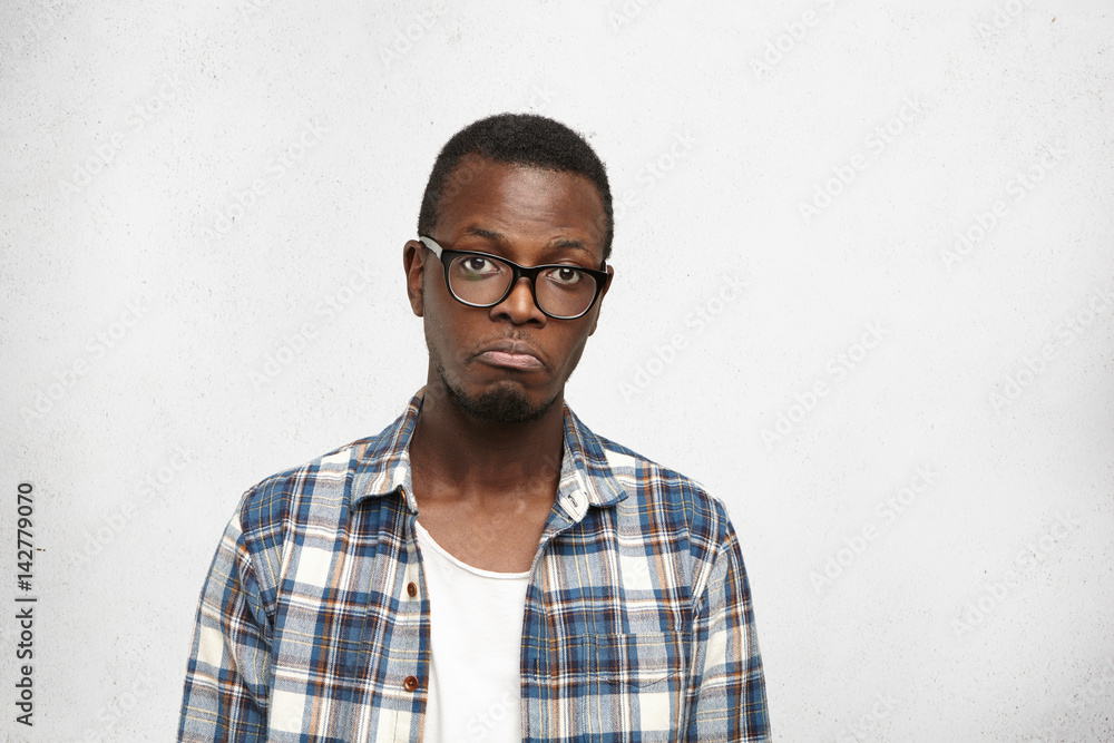 Sad young Afro-American man in trendy shirt and eyeglasses screwing up ...