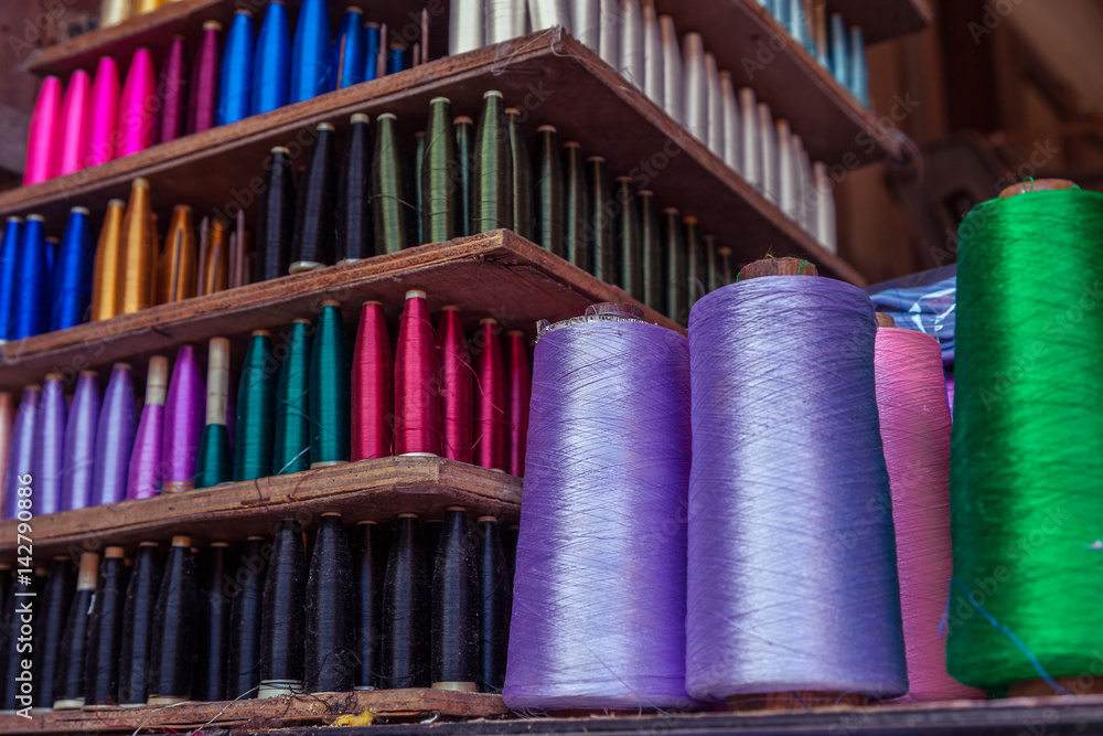 Colorful sewing thread spool arranged on wooden shelf ready to use in ...