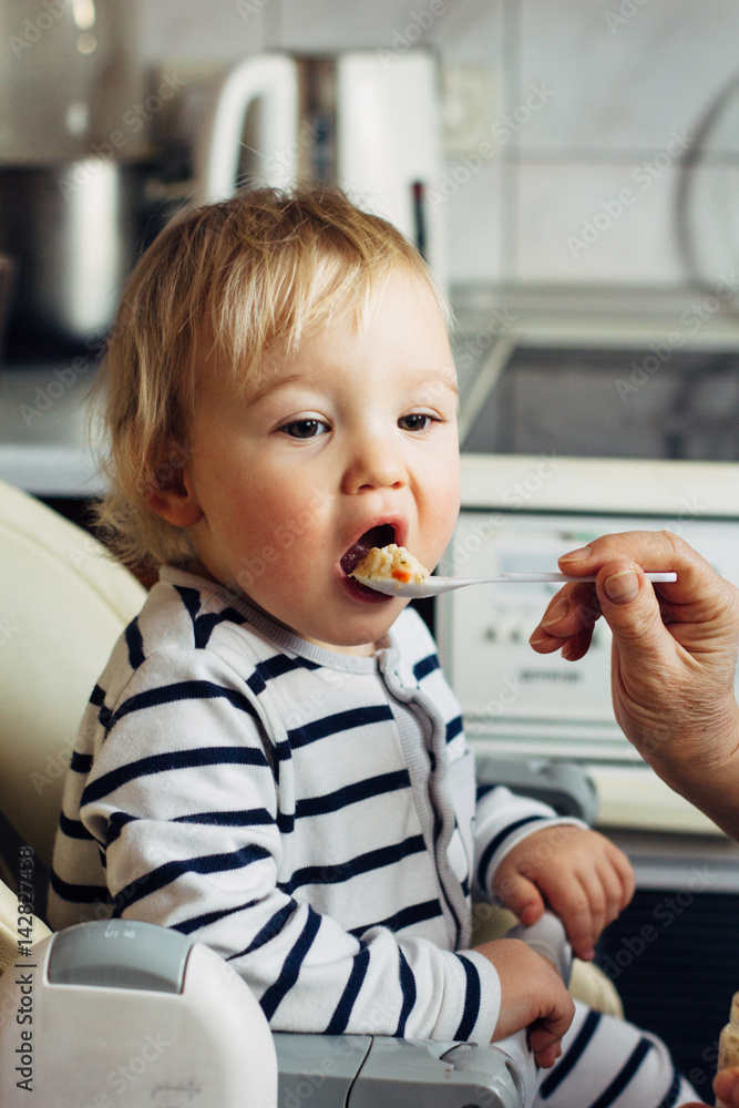 mom giving homogenized food to her son on high chair. Vertical shape ...