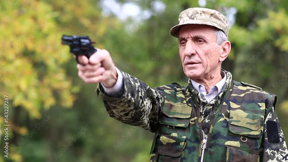 Senior man in military uniform shoots a revolver. Man with black gun ...