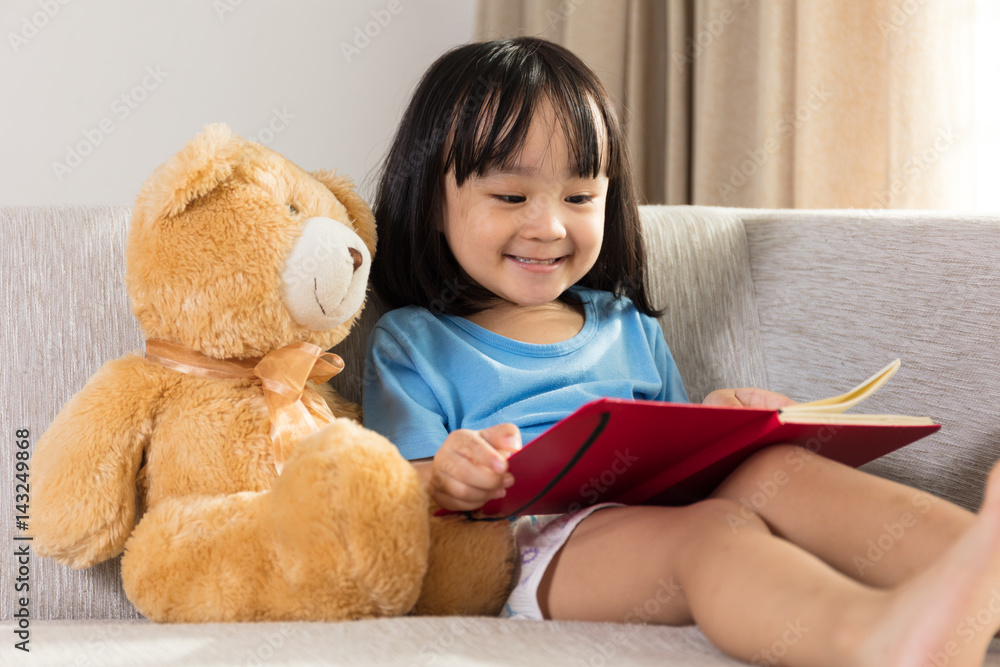 Smiling Asian Chinese little girl reading book with teddy bear Stock ...