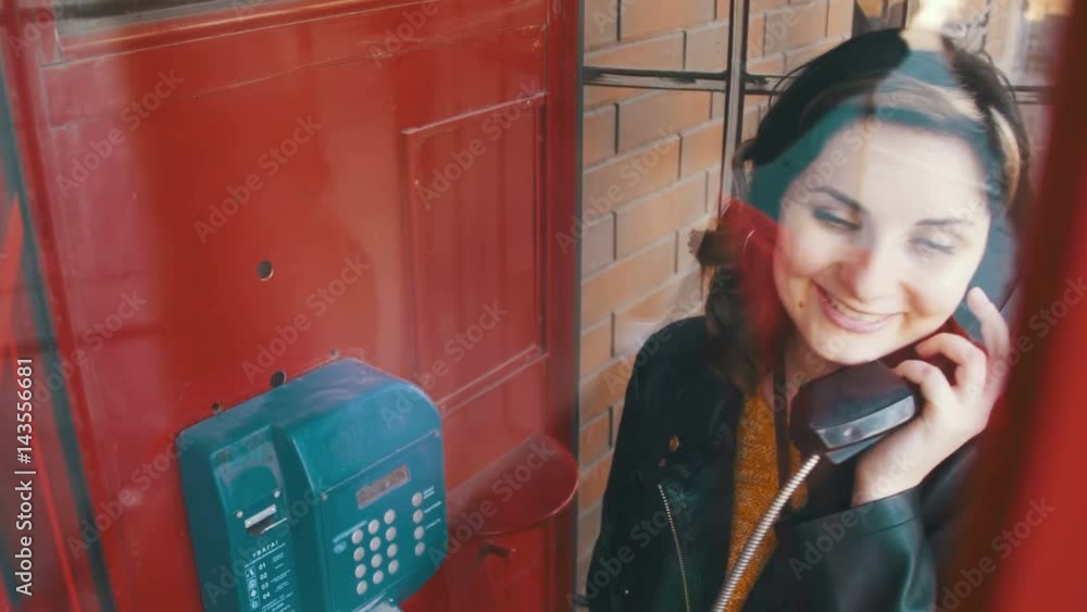 Happy girl in a red telephone booth talking on the phone in the street ...