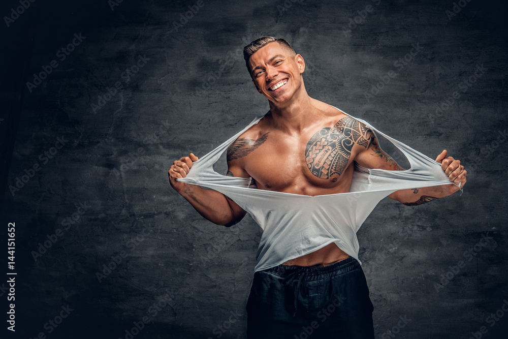A man with tattoo ripping t shirt on his chest. Stock Photo | Adobe Stock