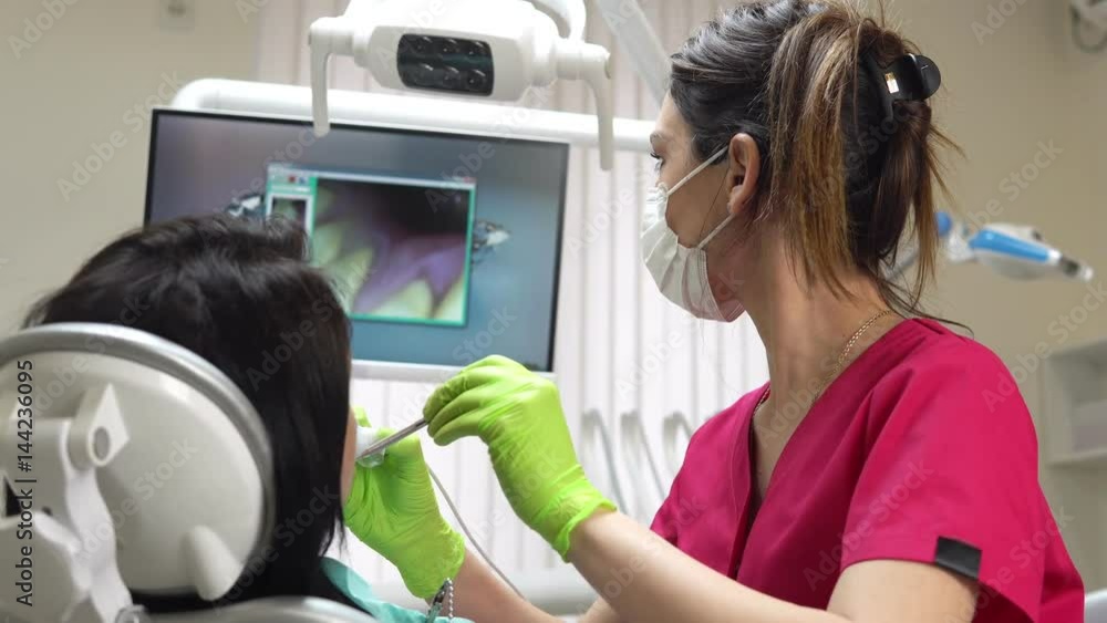 Young female dentist examining the mouth of a patient with an intraoral ...