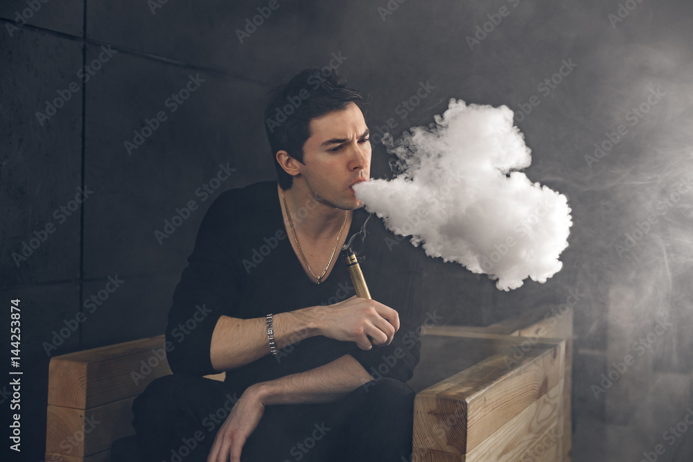 Vaping man holding a mod. A cloud of vapor. Black background. Smoking ...