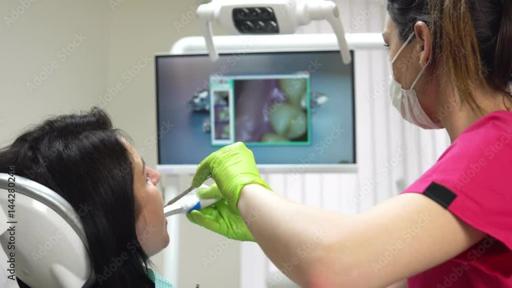Young female dentist examining the mouth of a patient with an intraoral ...