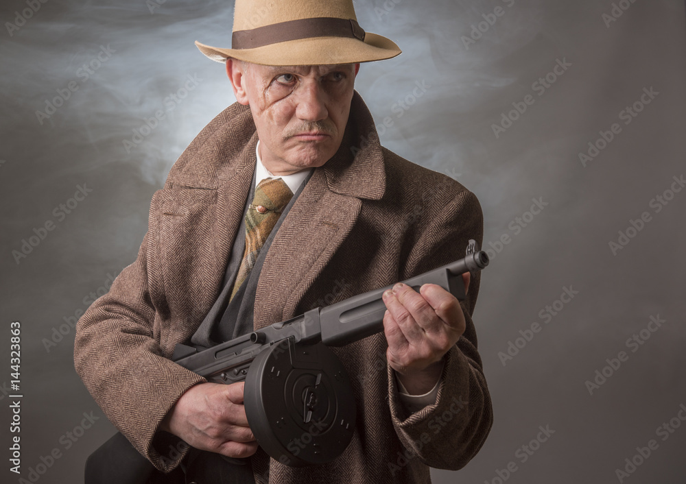 1940s male gangster holding a machine gun, on a grey smoky background ...