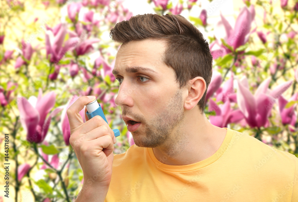 Young man using inhaler during asthmatic attack, on white background ...
