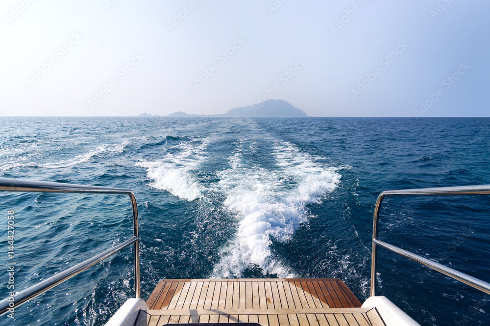 Trace of a wave with foam on the sea behind the boat. Wooden platform ...
