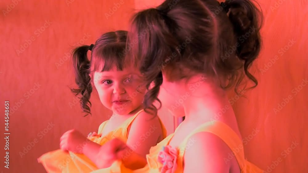 An angry child looks in the mirror. A beautiful little girl in a yellow ...