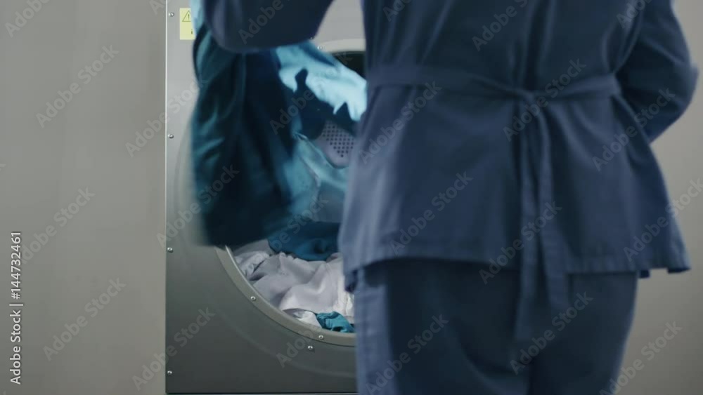 Female worker doing laundry. Pick up uniform from washing drum. Woman ...
